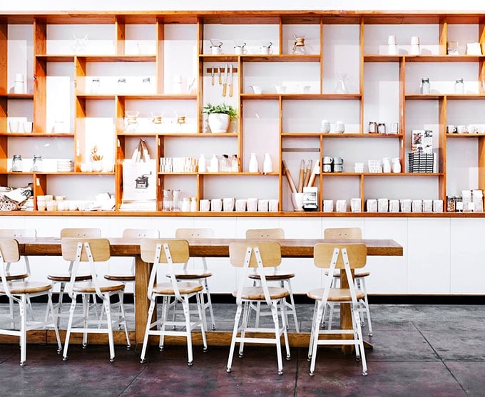 Shelves that could double as a pottery exhibition, framing a communal table where strangers become friends over the shared religion of good bread.