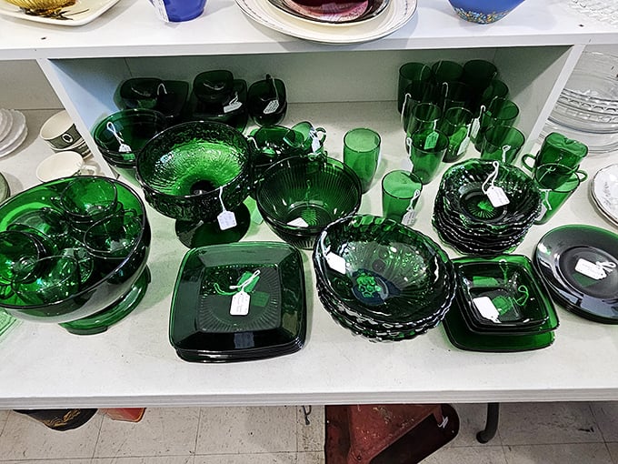 Emerald Depression glass gleams like jewels under the lights. Each piece survived the Great Depression and countless family dinners to reach this shelf. 