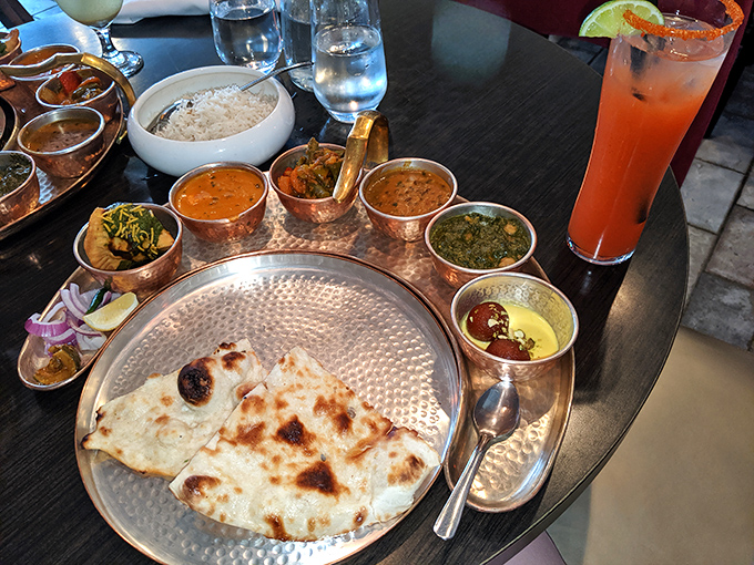 A copper-clad feast fit for royalty&mdash;curries in their burnished vessels surrounding freshly baked naan on a hammered silver platter, with a sunset-colored cocktail standing guard.