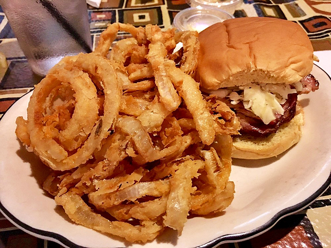 Golden onion rings tower beside a hearty pork sandwich, proving that some combinations are simply meant to be together.