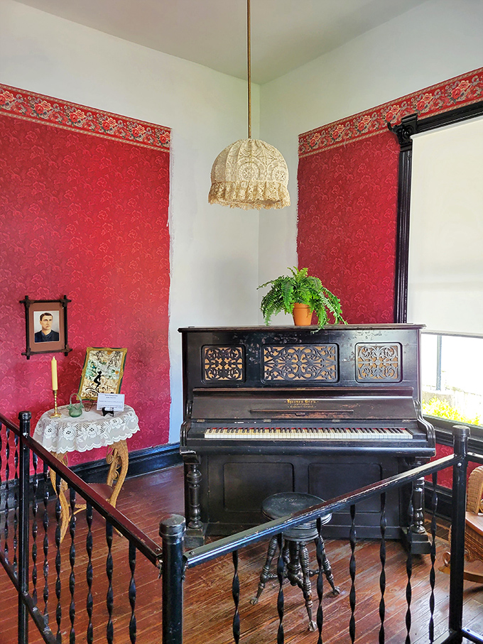 The parlor piano, surrounded by rich red wallpaper, stands ready to play the soundtrack of a bygone era when families made their own entertainment.