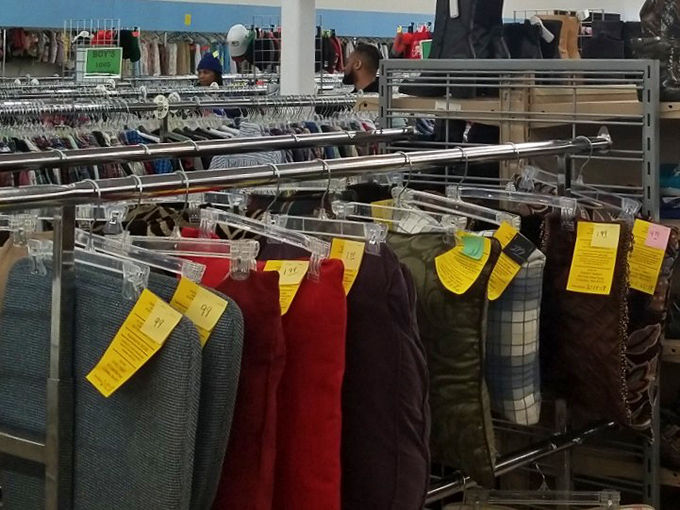 Color-coded tags mark potential treasures like trail markers in a bargain forest. Each hanger holds not just clothing, but stories waiting for new chapters to begin.