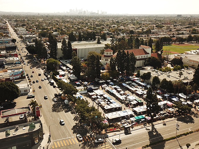 An aerial view of a bustling outdoor market in  Melrose Trading Post, where rows of vendor tents and historic buildings create a lively weekend scene under the sunny sky.