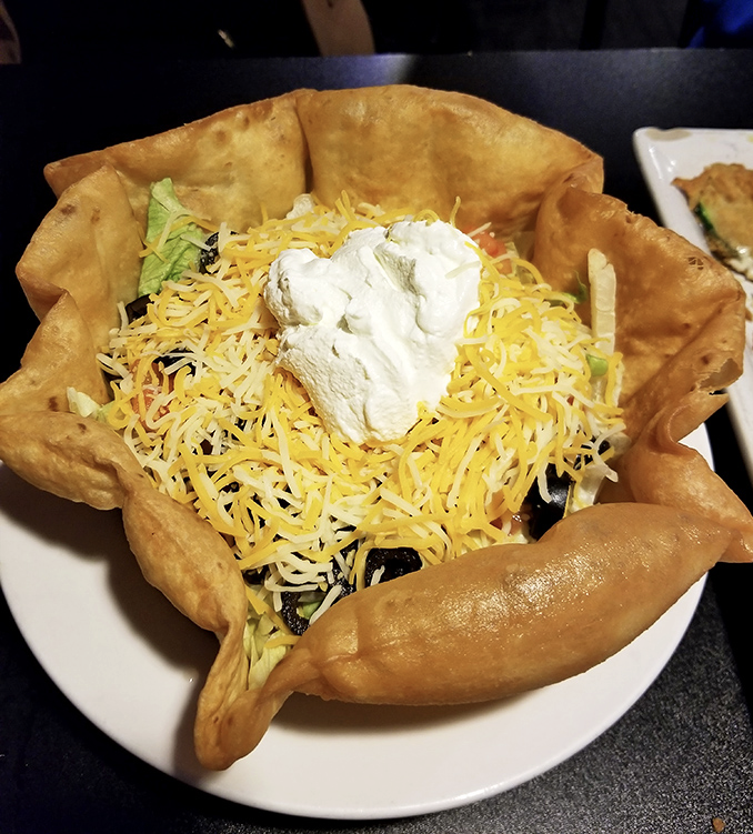The taco salad arrives in its own edible fortress, a crunchy moat protecting a kingdom of cheese, veggies, and pure satisfaction.