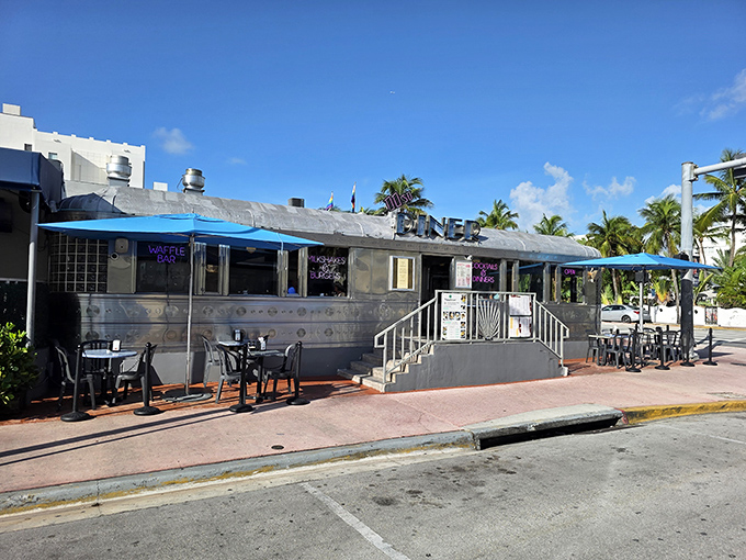 The gleaming stainless steel exterior of 11th Street Diner catches Miami's sunshine like a chrome beacon from another era, complete with turquoise umbrellas for shade.