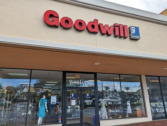 The iconic red Goodwill sign beckons like a lighthouse for bargain hunters. Behind those doors, treasures await the patient and persistent.