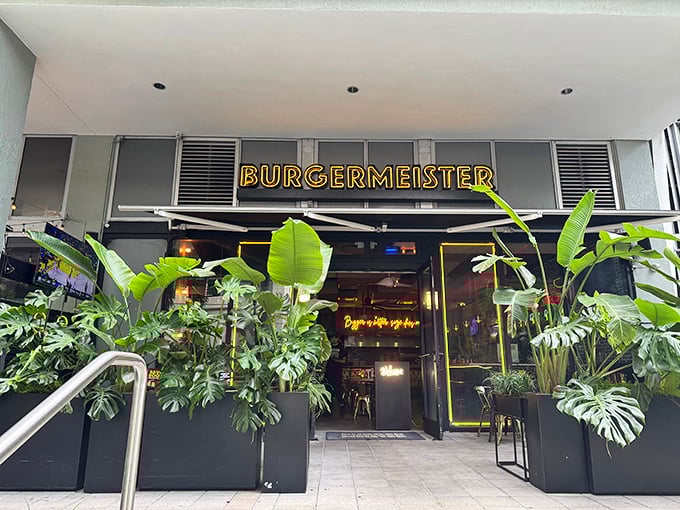 Burgermeister's entrance beckons with lush tropical plants and glowing yellow signage &ndash; like nature and neon joined forces to guide hungry humans home.