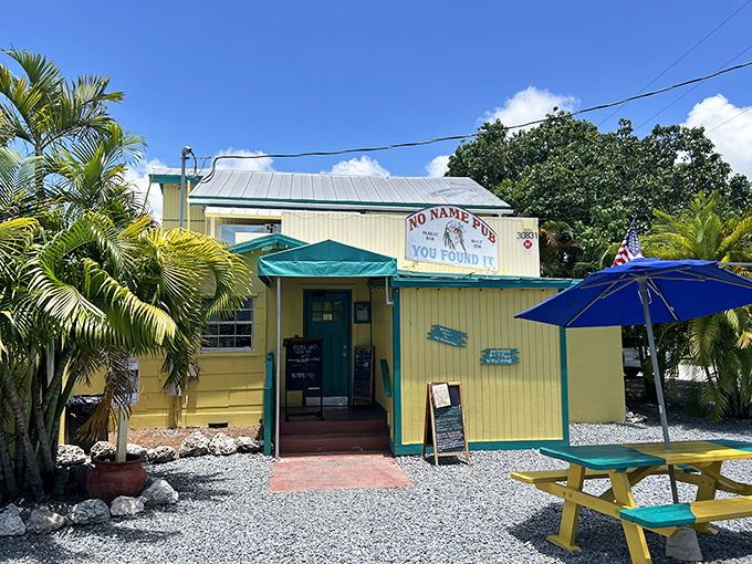 The cheerful yellow exterior of No Name Pub stands like a tropical beacon among the palms, promising cold beer and hot stories inside.