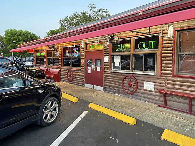The log cabin exterior of Shiver's BBQ stands as a rustic beacon of hope for hungry travelers, its neon "OPEN" and "TAKE OUT" signs promising smoky salvation.