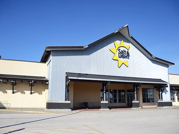 The distinctive yellow sun logo of Salt & Light Thrift shines like a beacon of bargain hope against the corrugated metal exterior, promising treasures within.