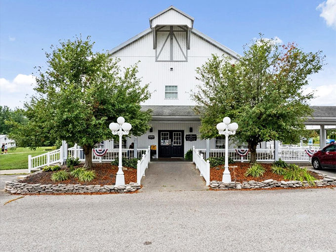 The white barn-like exterior of Gasthof welcomes visitors like a warm handshake, promising authentic Amish hospitality beneath those towering shade trees.