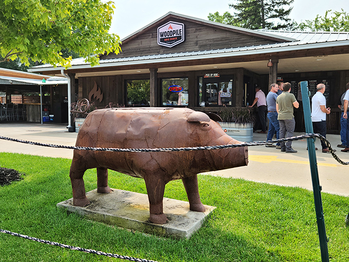The rustic charm of Woodpile BBQ Shack welcomes hungry visitors with its wooden exterior and metal roof, complete with a pig statue standing guard.
