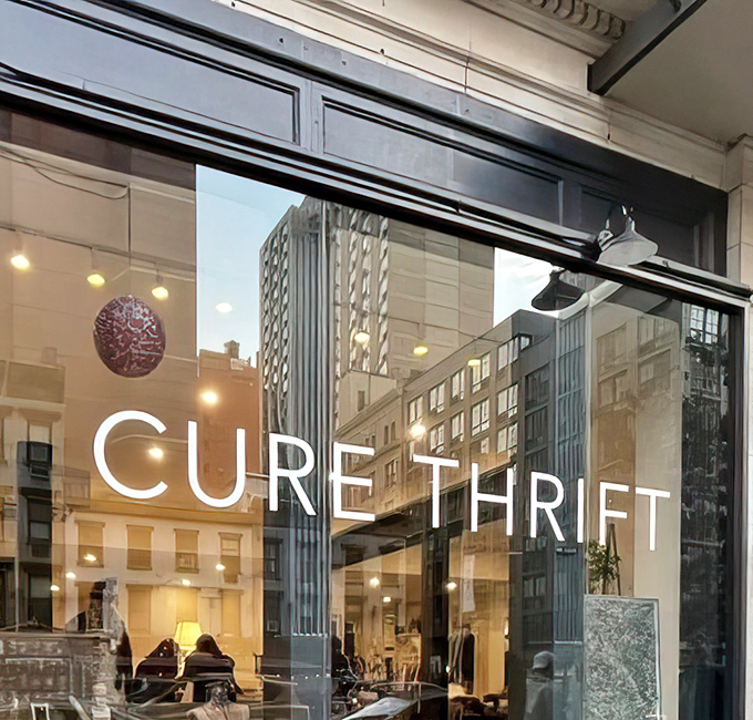 The sleek black exterior of Cure Thrift beckons passersby with its elegant signage and inviting window displays, promising treasures within.