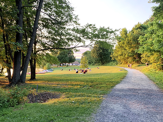Golden light spills across Marsh Creek Lake as visitors lounge on the grassy shore, savoring a tranquil Pennsylvania sunset surrounded by nature&rsquo;s gentle calm.