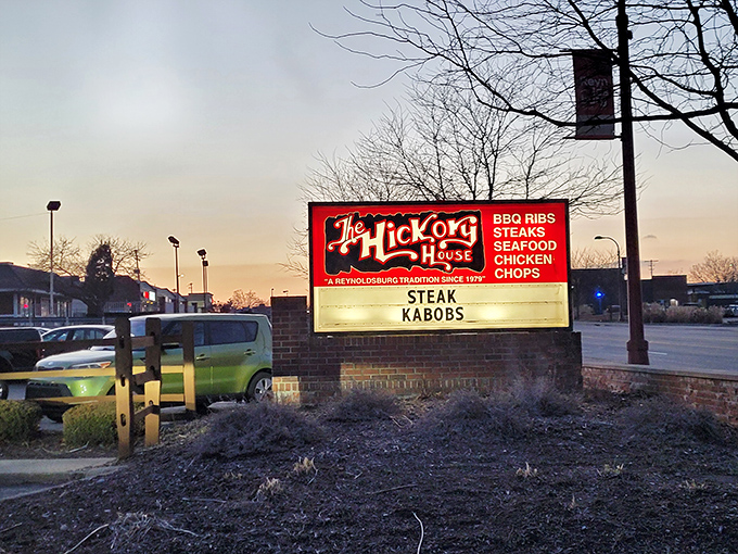 The iconic red sign of Hickory House glows at dusk, a beacon for hungry travelers promising BBQ ribs, steaks, and a Reynoldsburg tradition since 1979.