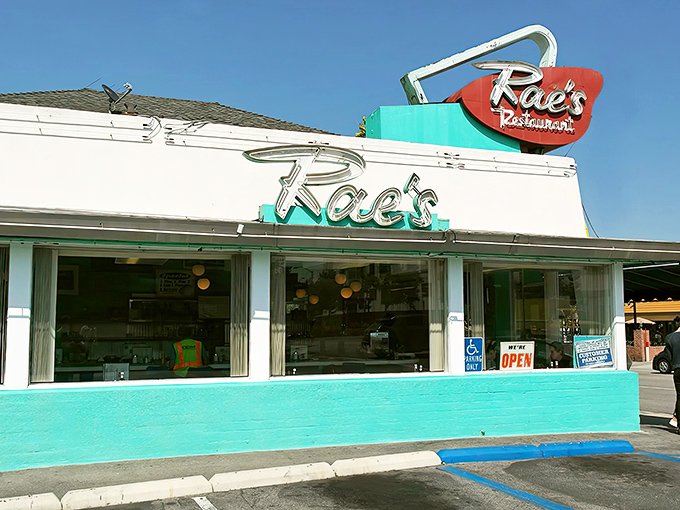 The iconic Rae's sign beckons like a turquoise-trimmed time machine, promising comfort food that predates your smartphone addiction.