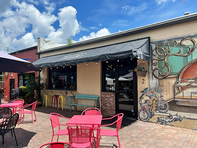 A second view of the welcoming fa&ccedil;ade, where pink chairs pop against the beige building and a mural hints at the creativity waiting inside.
