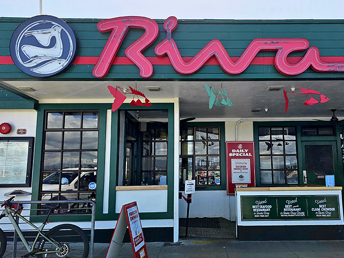 The iconic green exterior and neon-red sign of Riva Fish House stands like a beacon for seafood lovers wandering Santa Cruz Wharf.