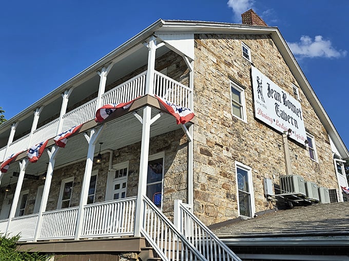 The Jean Bonnet Tavern stands proudly against a blue Pennsylvania sky, its historic stone walls and white balconies whispering tales from America's earliest days.