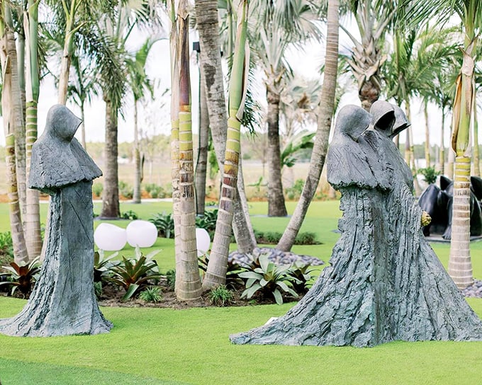 The mysterious hooded figures stand like silent sentinels among swaying palms, creating an atmosphere that's equal parts enchanting and delightfully eerie.