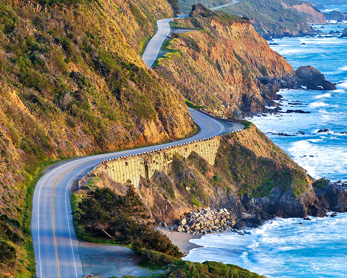 Highway 1 curves like nature's rollercoaster, hugging the dramatic California coastline as waves crash below in a breathtaking display.