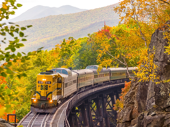 The iconic yellow locomotive crosses Frankenstein Trestle, surrounded by New Hampshire's breathtaking autumn foliage in the White Mountains.