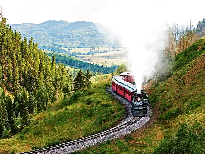 Steam billows dramatically as the historic locomotive navigates a mountain curve, painting a scene straight from a Western film's most breathtaking moment.