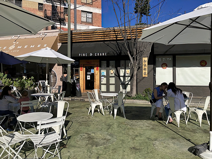 The welcoming exterior of Pine & Crane beckons with promise, where outdoor seating under white umbrellas offers the perfect spot for savoring those legendary dan dan noodles.
