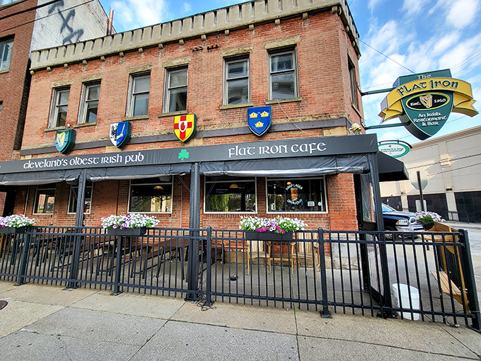 The historic brick facade of Flat Iron Cafe stands proudly in Cleveland's Flats district, complete with colorful heraldic shields announcing its Irish heritage.