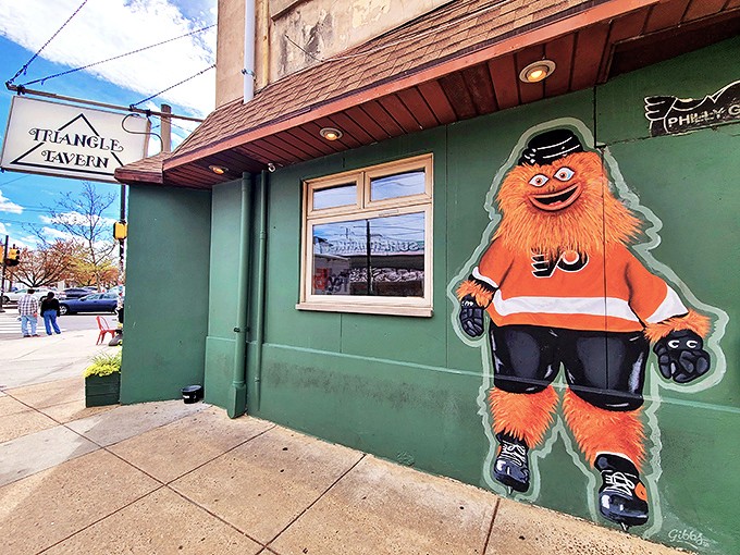 Gritty, Philadelphia's beloved orange mascot, stands guard outside Triangle Tavern &ndash; a quirky sentinel promising good times and great wings within.