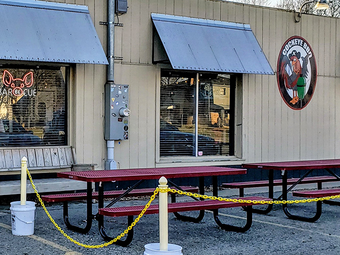 The unassuming exterior of Cockeye BBQ proves once again that in barbecue, flashy facades are inversely proportional to meat quality. Those red picnic tables await your smoky adventure.