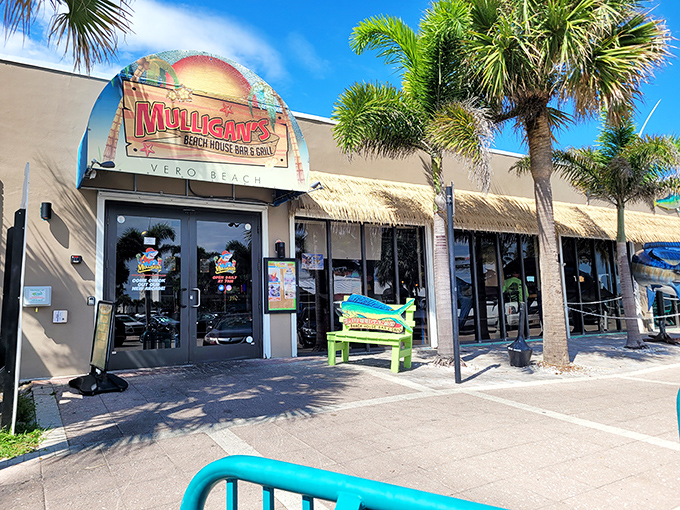 The cheerful facade of Mulligan's Beach House beckons like a tropical mirage, promising seafood treasures and ocean breezes just beyond those palm-flanked doors.