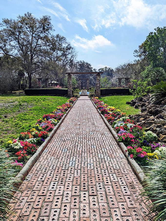 A brick pathway lined with vibrant flowers leads to stone archways, like a royal garden entrance that whispers of Depression-era craftsmanship and Florida's surprising formal garden heritage.