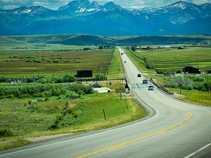 Nature's version of a red carpet, rolling out between emerald fields and snow-capped peaks. The Tetons stand guard like celebrities at a premiere.