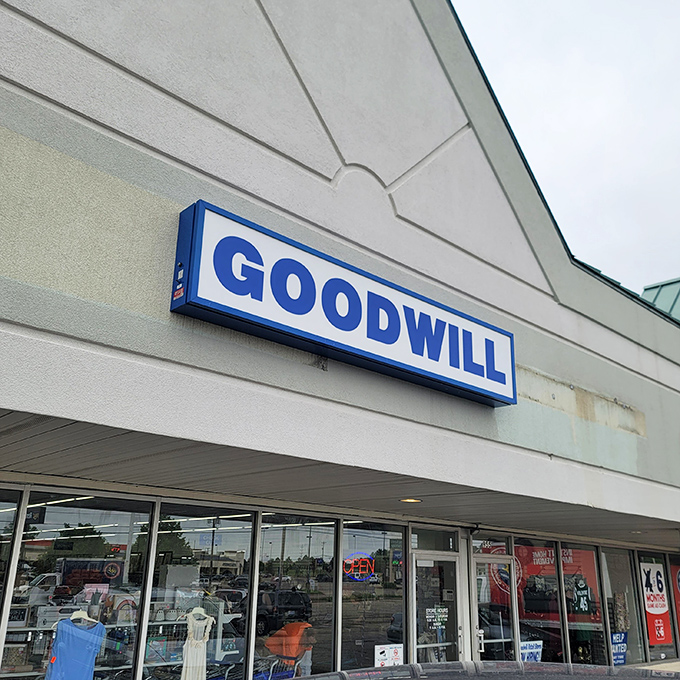 The iconic blue Goodwill sign beckons like a lighthouse for treasure hunters &ndash; promising adventures in secondhand splendor behind those unassuming walls.