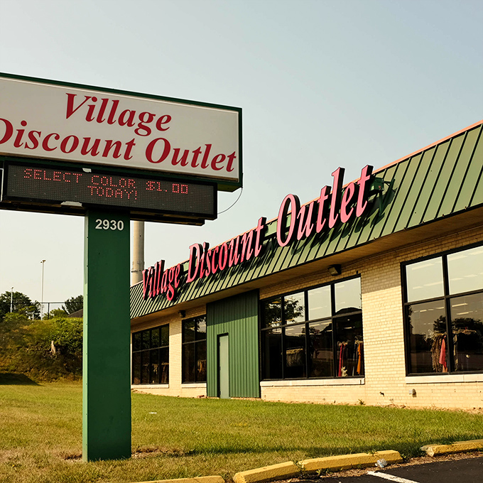 The iconic red signage beckons like a lighthouse for bargain hunters. Village Discount Outlet's exterior promises treasures within for those brave enough to explore.