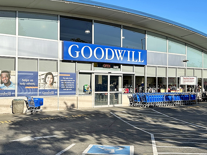 The blue Goodwill sign beckons like a lighthouse for bargain hunters, with shopping carts standing ready for treasure-seeking missions.