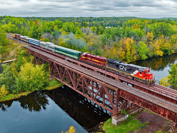 Engineering marvel meets Minnesota wilderness as this vintage train crosses a rusted iron trestle, reflecting perfectly in the mirror-like waters below.