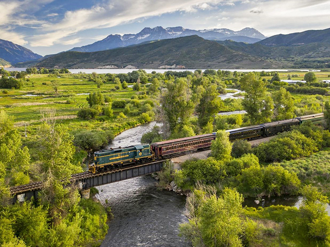 Nature's perfect postcard: The Heber Valley Railroad winds through lush greenery with mountains standing guard like ancient sentinels.