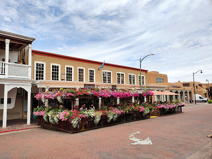 Santa Fe's historic Plaza Café blooms with vibrant flowers during summer, its outdoor patio a colorful oasis amid the adobe architecture.