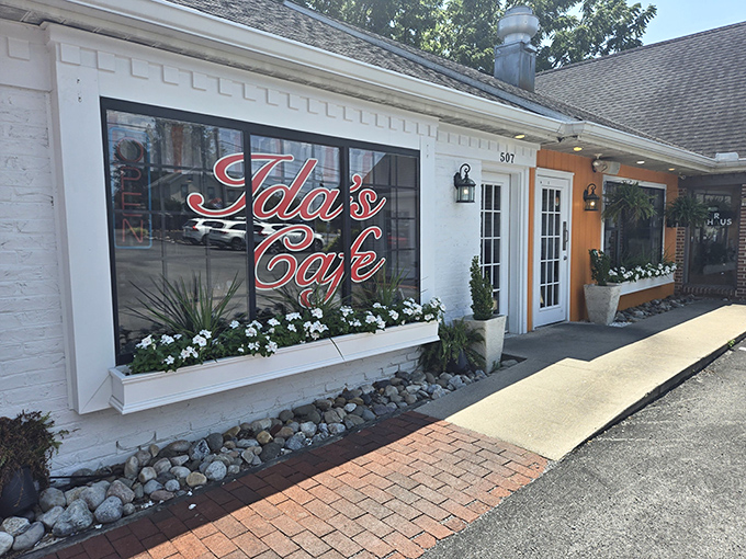 Ida's Cafe welcomes you with a pristine white exterior, vibrant red signage, and flower boxes that say "comfort food lives here" before you even step inside.