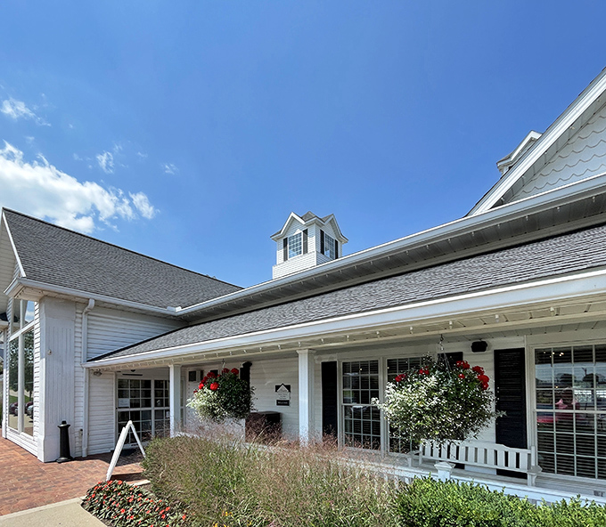 Blue skies frame this pristine white farmhouse structure, where hanging flower baskets add splashes of color to an already picture-perfect entrance.