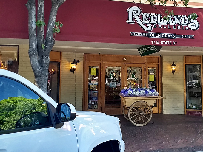 The welcoming facade of Redlands Galleria beckons treasure hunters with its vintage cart display and warm wooden entrance. Time travel begins here!