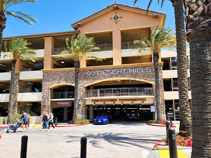 The grand entrance to Desert Hills Premium Outlets stands like a desert mirage, promising retail therapy under swaying palm trees and California sunshine.