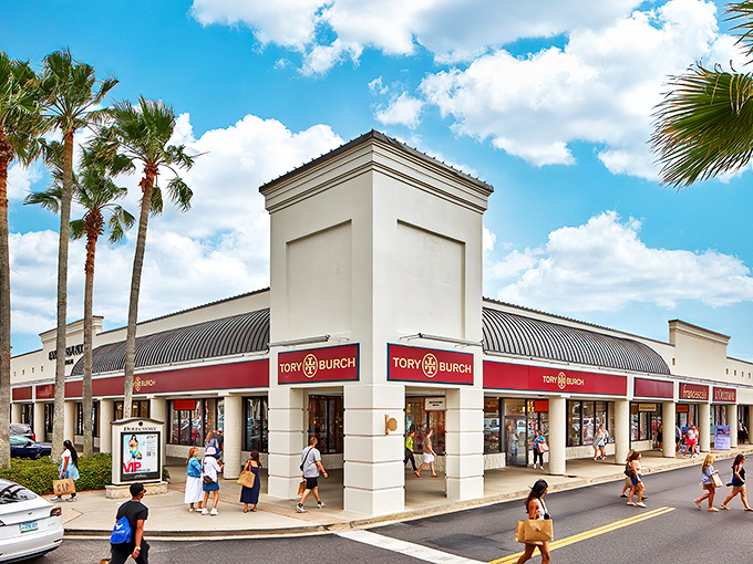 The iconic Tory Burch storefront welcomes shoppers with its distinctive red awning, where palm trees and designer dreams coexist in perfect Florida harmony.
