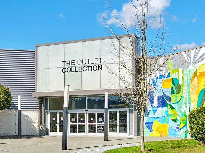 The sleek, modern entrance to The Outlet Collection Seattle promises retail adventures beyond those glass doors. Blue skies and colorful murals welcome bargain hunters.