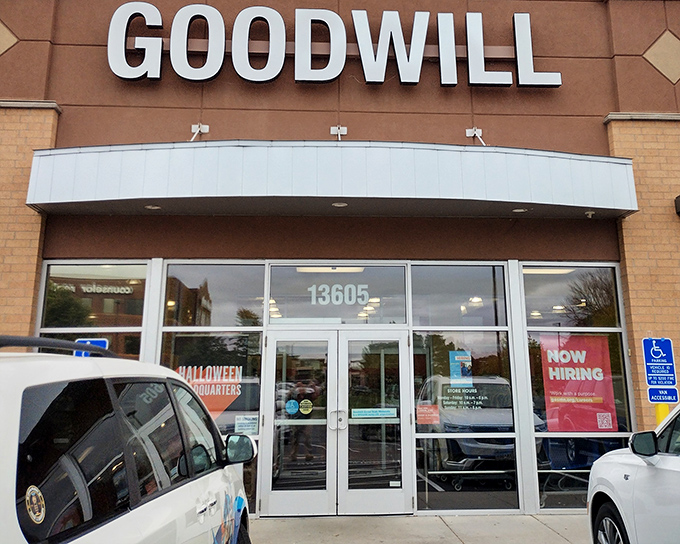 The familiar blue and white Goodwill sign beckons bargain hunters like a lighthouse guiding ships to treasure-filled shores. Halloween decorations hint at seasonal treasures waiting inside.
