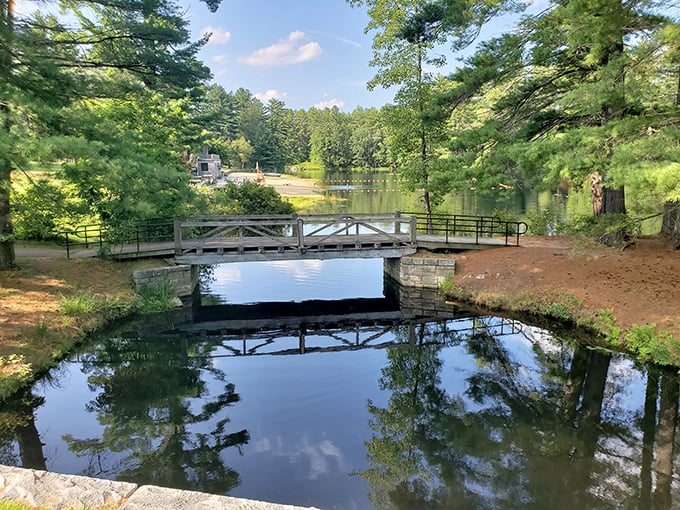 A wooden footbridge creates the perfect postcard moment at Bear Brook State Park, where reflections double the beauty and halve your stress levels.