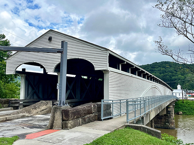 The Philippi Covered Bridge stands proudly against West Virginia's rolling hills, a white-washed time traveler still carrying modern traffic after nearly two centuries of service.
