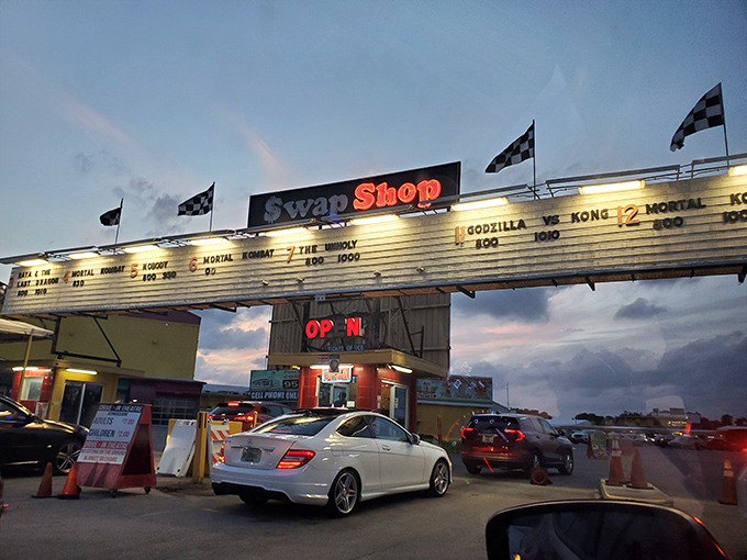 As dusk settles, the Swap Shop's drive-in marquee lights up with movie titles, transforming from daytime bargain hunter's paradise to nighttime cinema under the stars.